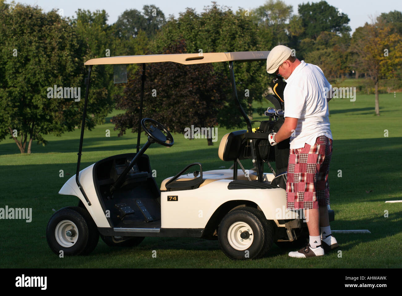 American golfer man with golf clubs in bag and a golf cart on the golf ...