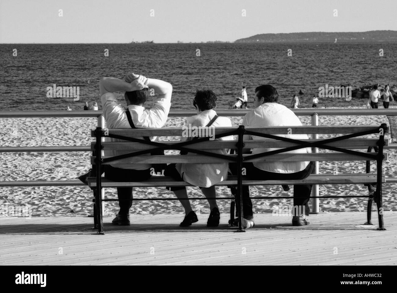 people enjoying a warm sunny day on a boardwalk park bench at the beach ...