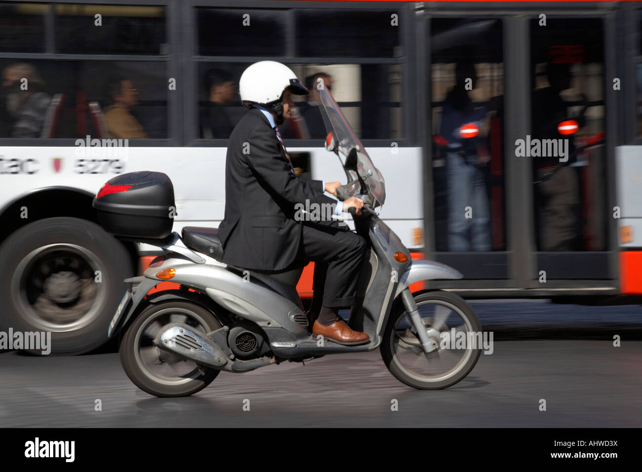 Business man in suit and white helmet on scooter commutes past bus full ...