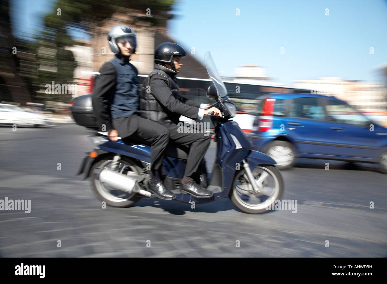 Scooter with driver and pillion passenger speeds past through Piazza ...