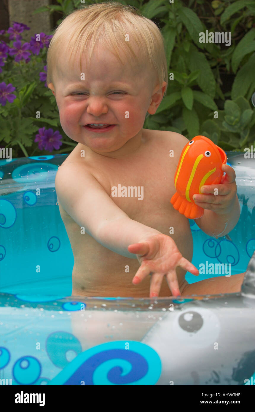 Toddler playing with toy fish in water filled paddling pool in family ...