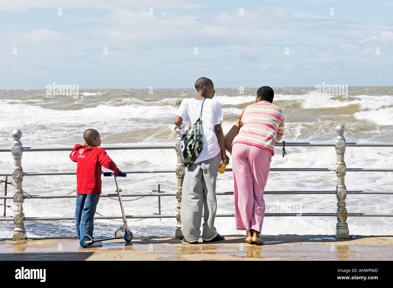 Family of three watching the surf roll in on Blackpool seafront Stock ...