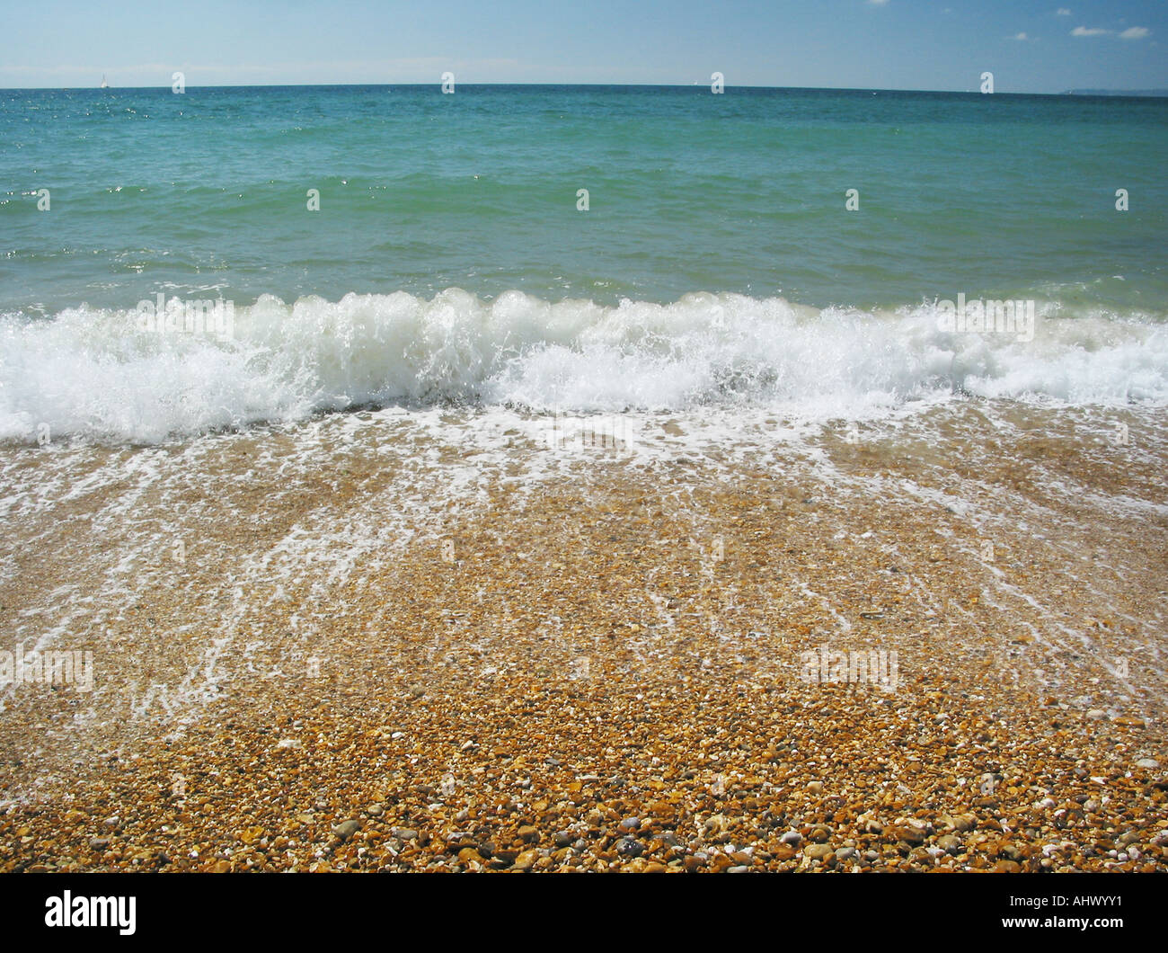 Coastal scene with pebbled beach, rolling waves and clear blue skies ...