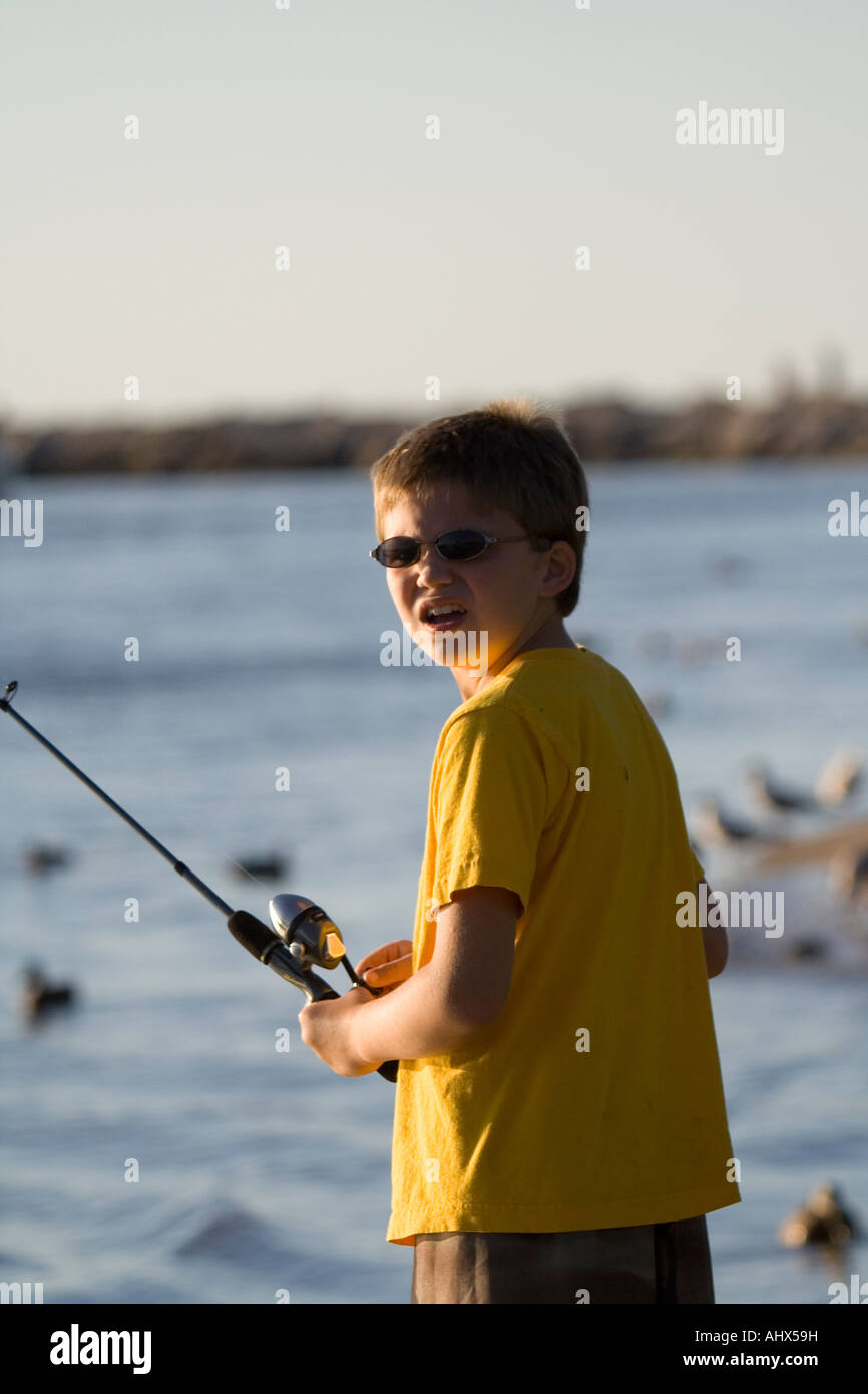 Young boy fishing alone by the water looking back over his shoulder and ...