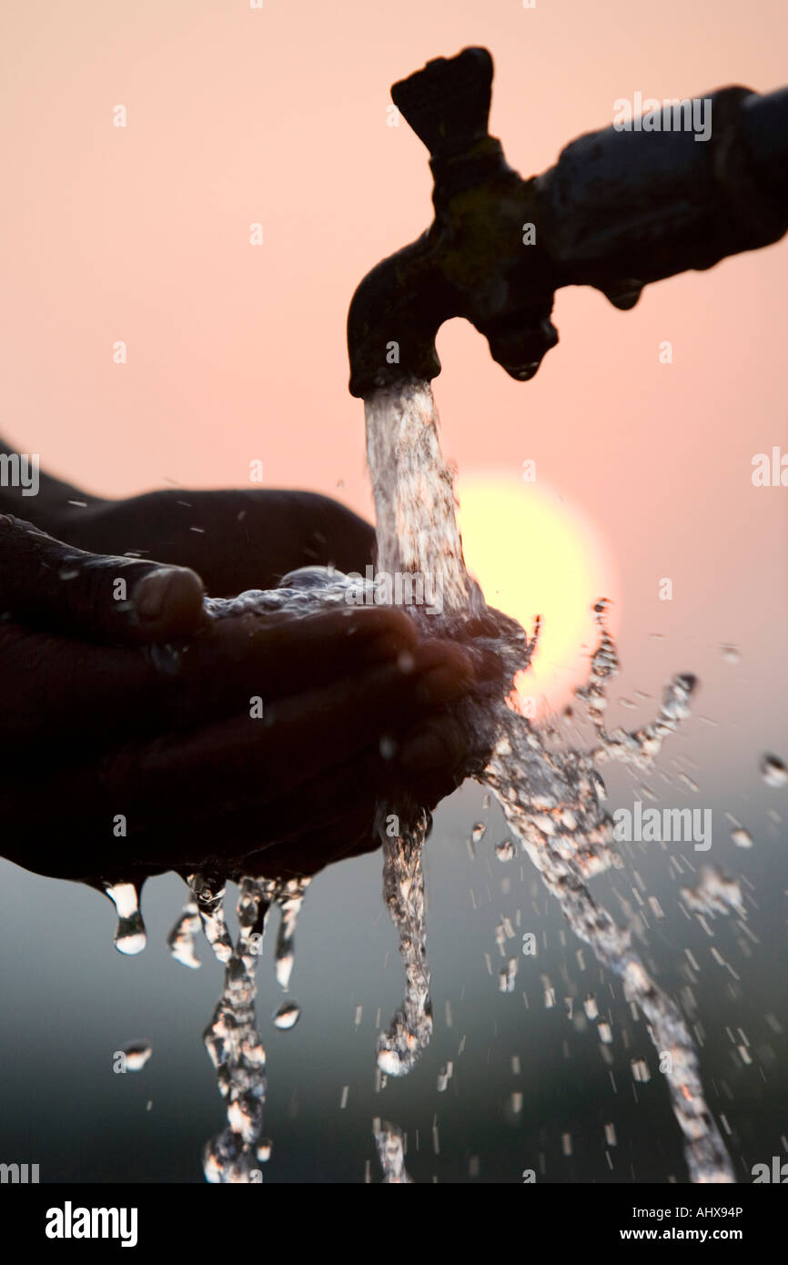 Cupped hands collecting water at a stand pipe tap at sunrise. India ...