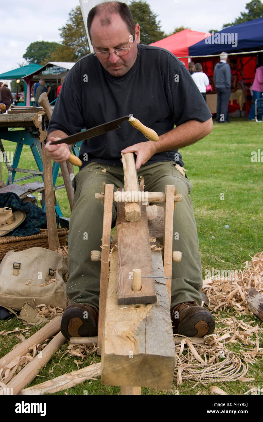 Bodger or woodworker seated on a shaving horse, using a drawknife to ...