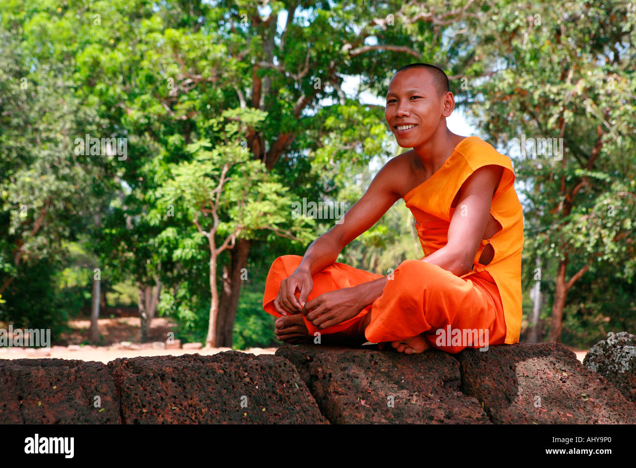 Buddhist monk relaxing on a wall at the temple of Bakong, Roluos Group ...