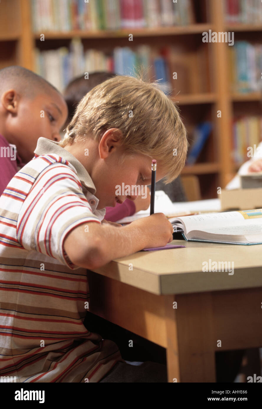 Caucasian male student writing book report in Elementary school library ...