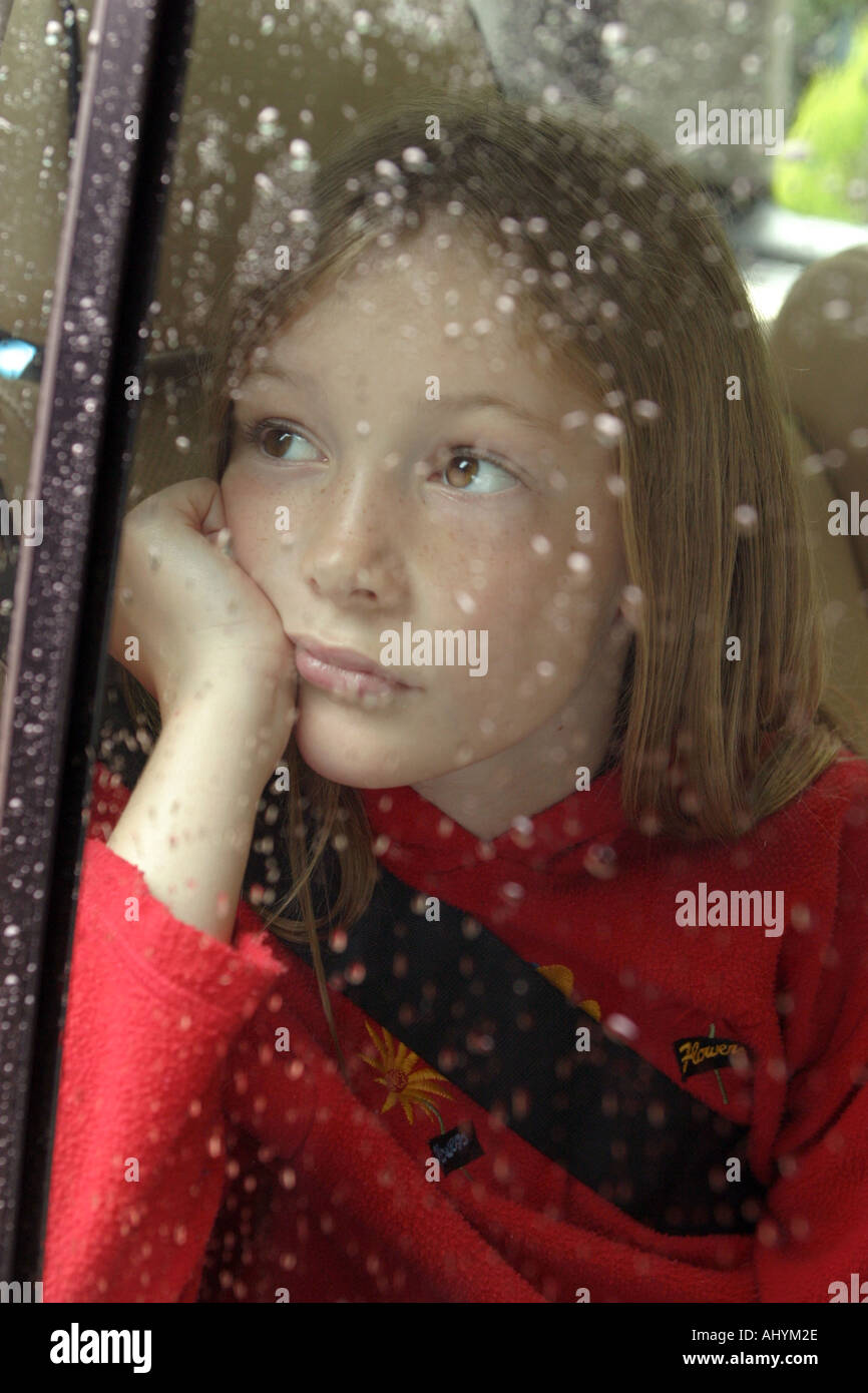 Young sad girl looking bored gazes through a rain covered car window ...