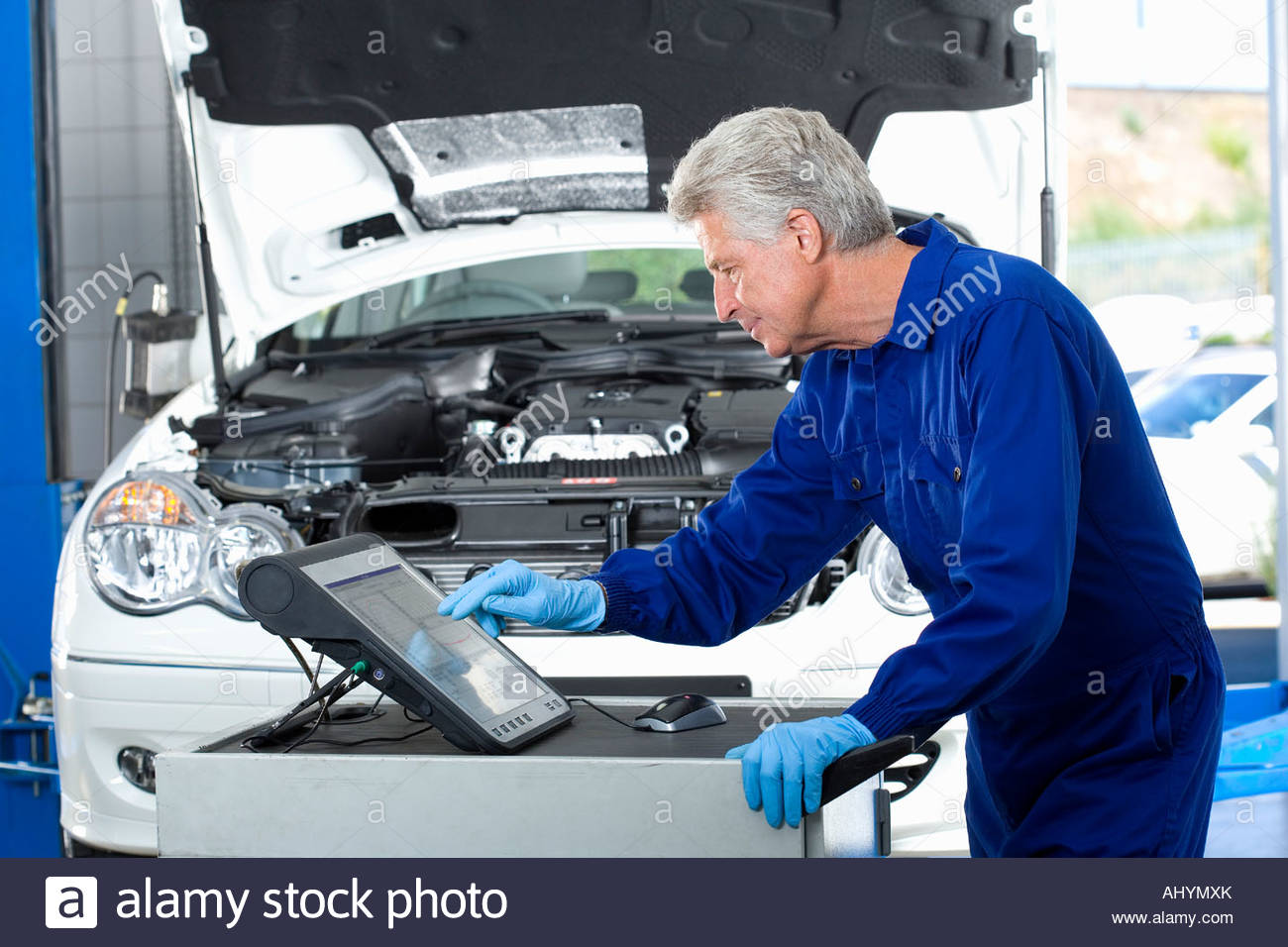 Mature car mechanic, in blue overalls, using computer in auto repair ...