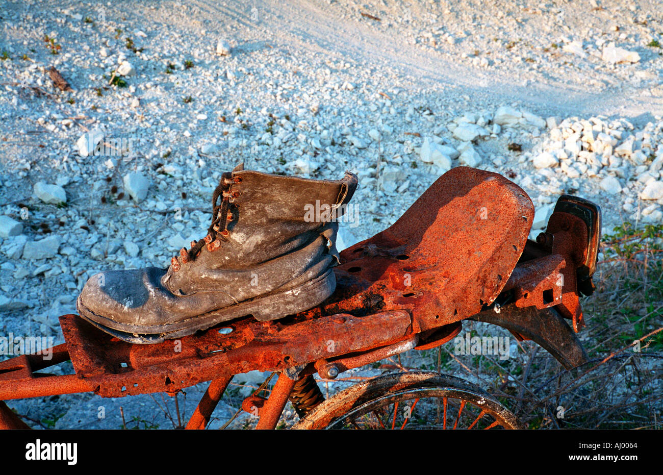Old leather work boot on pillion seat of burnt out rusty Kawasaki trail ...