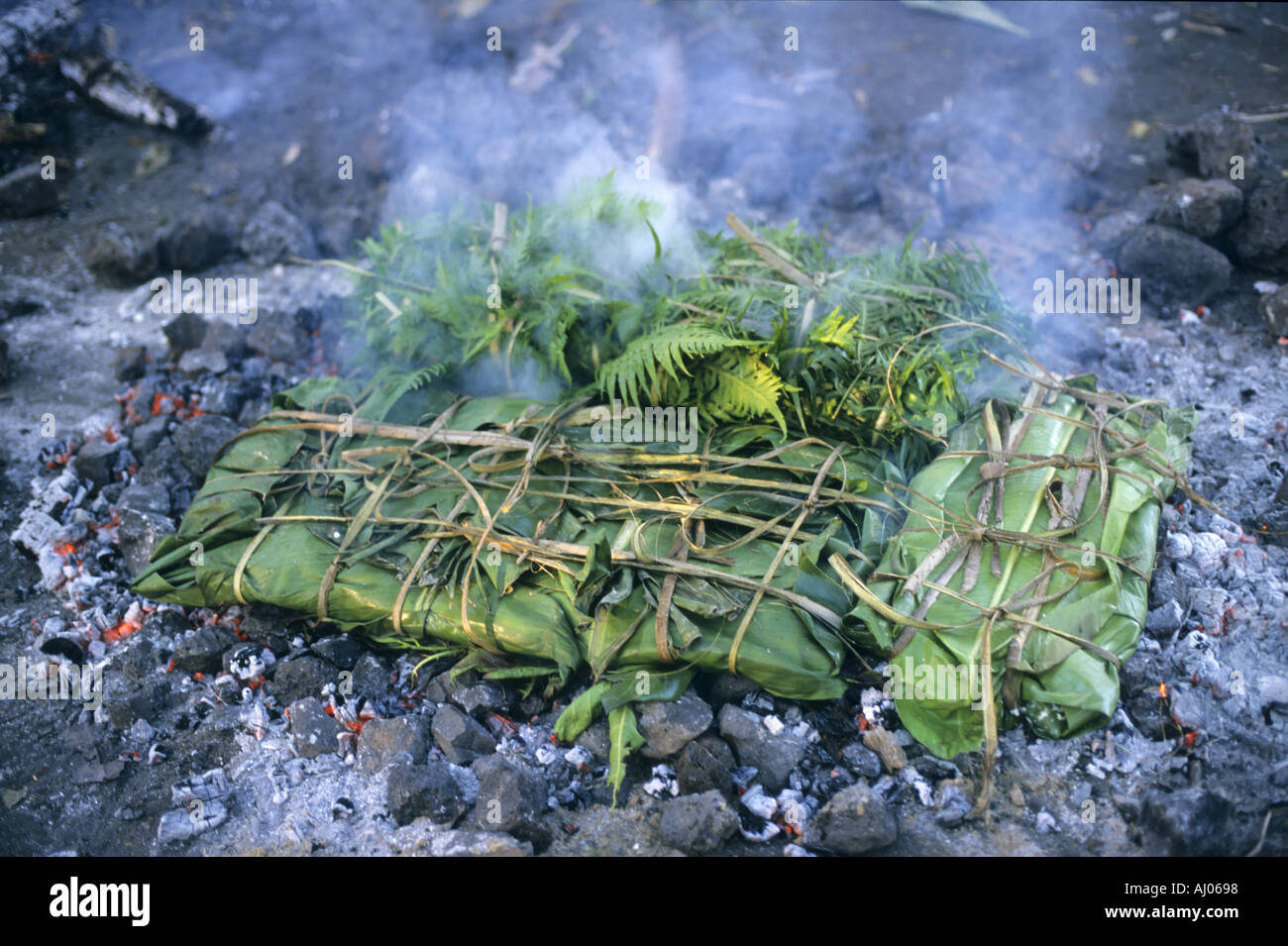 A laplap dish wrapped with bananas leaves being cooked on coals ...