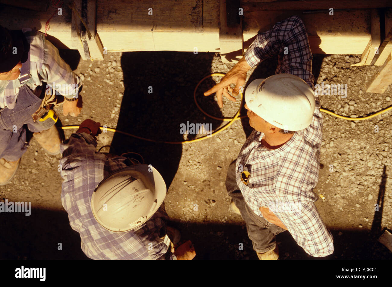 Overhead view of three hard hat wearing construction workers talking at ...