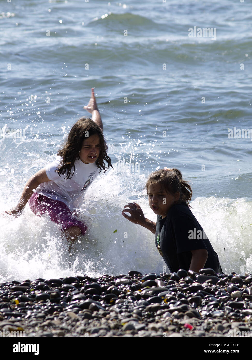 Two girls on the edge of the sea trying to escape being drenched by a ...