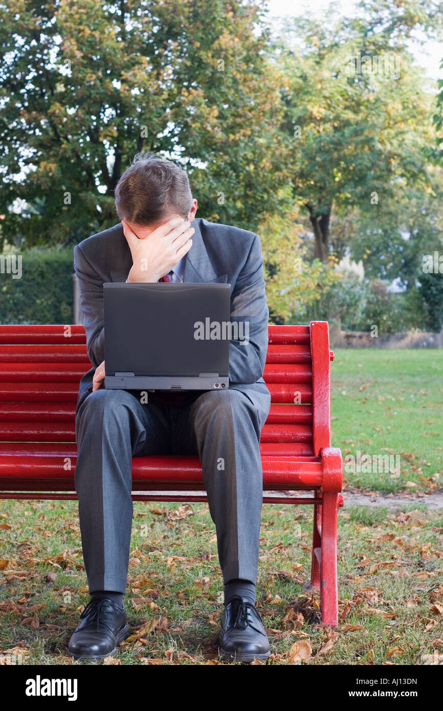 Tired businessman with laptop sitting on a park bench Stock Photo - Alamy