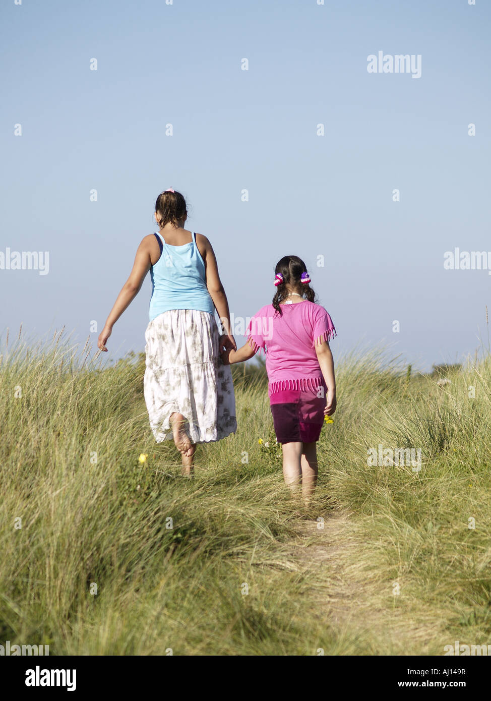 Teenage girl leading her younger sister along a sandy coastal path ...