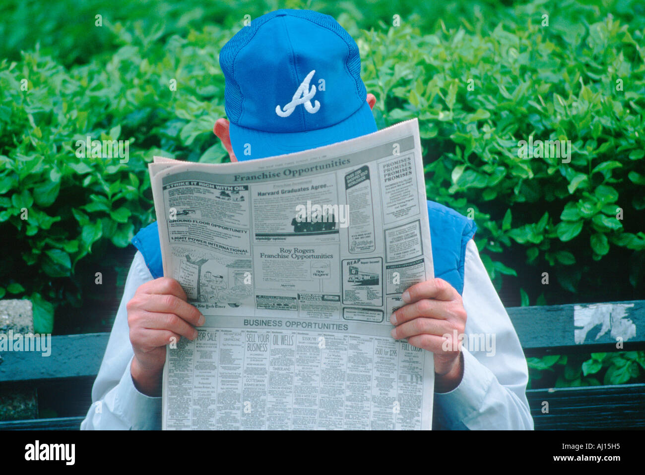 A man sitting on a bench reading the newspaper Stock Photo - Alamy