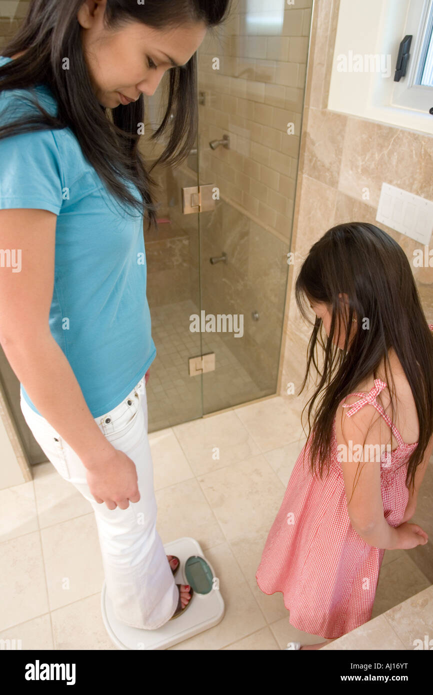 A mother stands on a weight scale while her daughter watches Stock ...