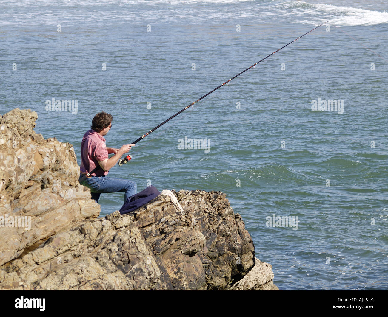 Brown haired man standing on a rock sea fishing Stock Photo - Alamy