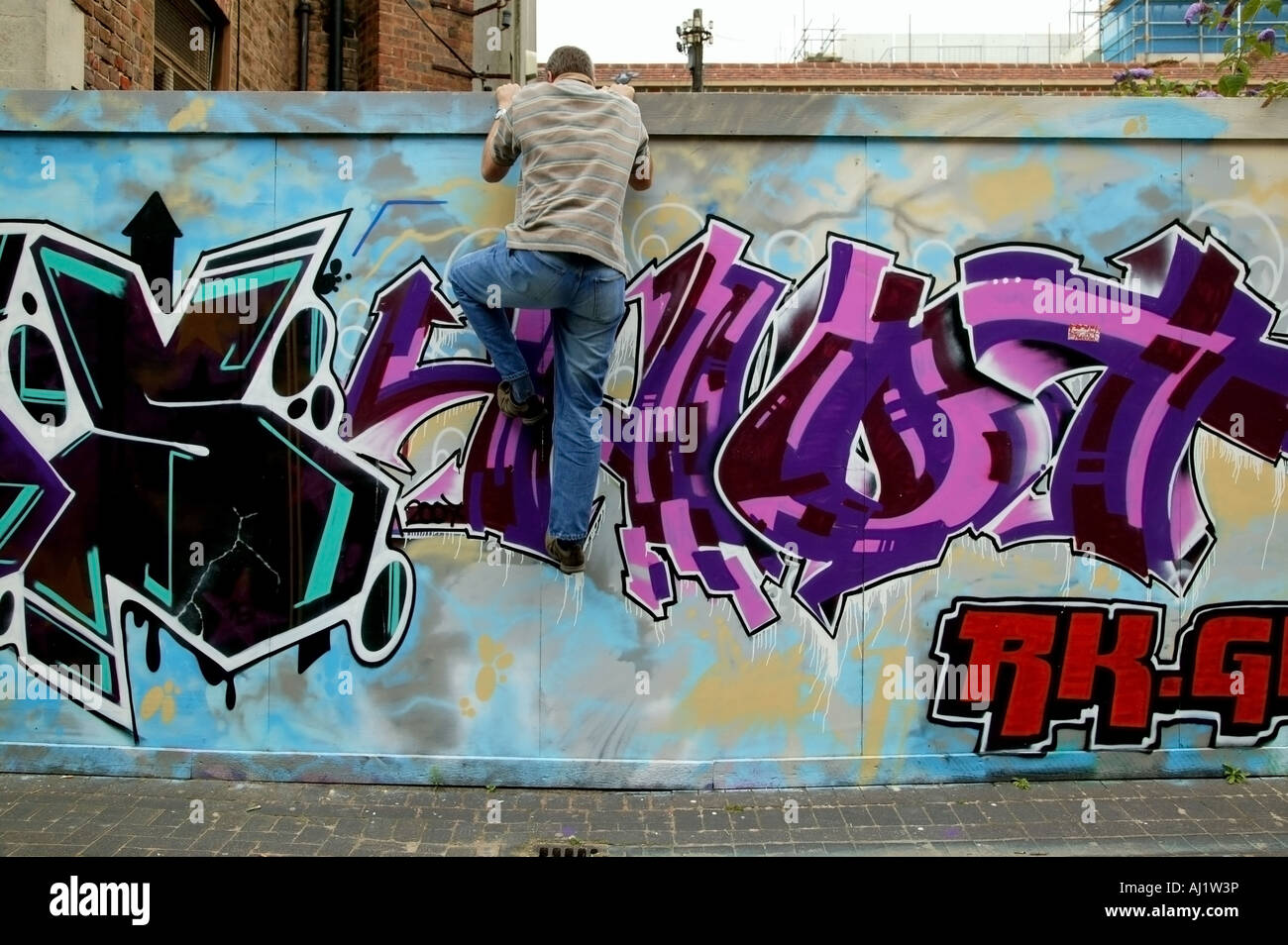 Agile young man climbing over a wall covered in graffiti Stock Photo ...