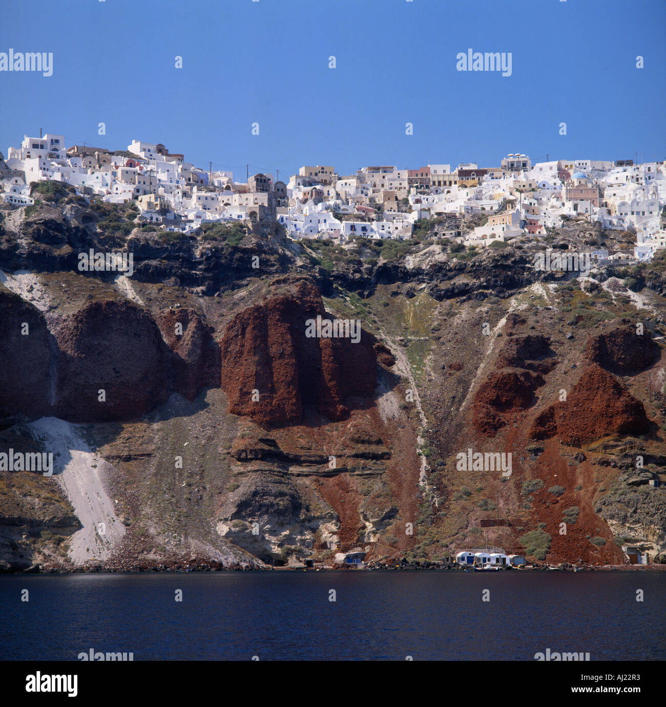 View from sea of Oia village spread along red barren volcanic cliff ...