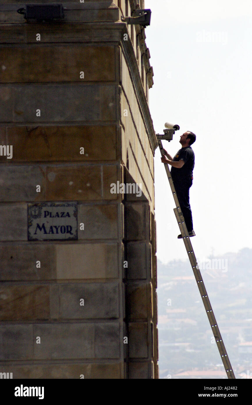 Man on ladder setting up a surveillance camera on an official building ...