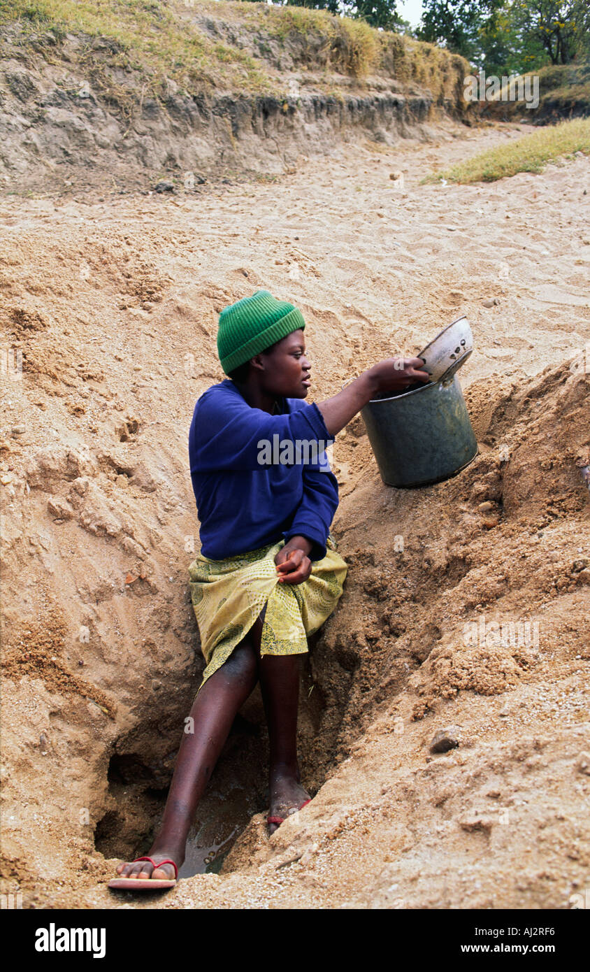 Young woman collecting the last dregs of water from a dry riverbed ...