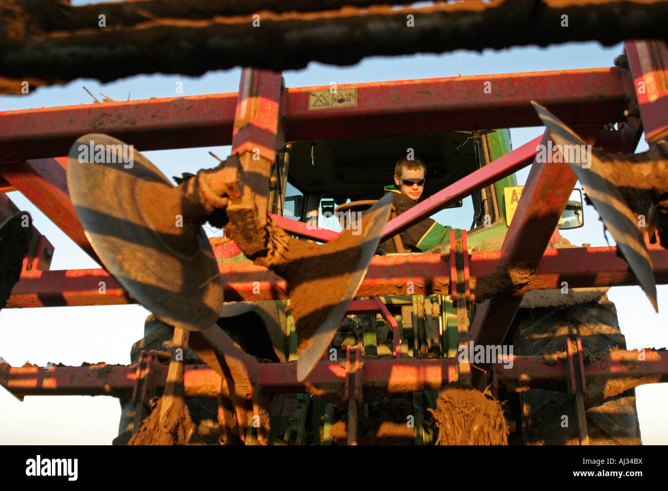 A Farmer driving a tractor looking back through a cultivator wearing ...