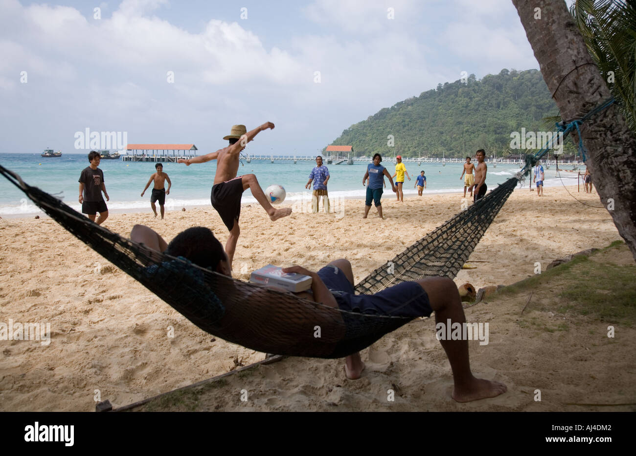 Tourist reading a book on the beach, and watching football/soccer game ...