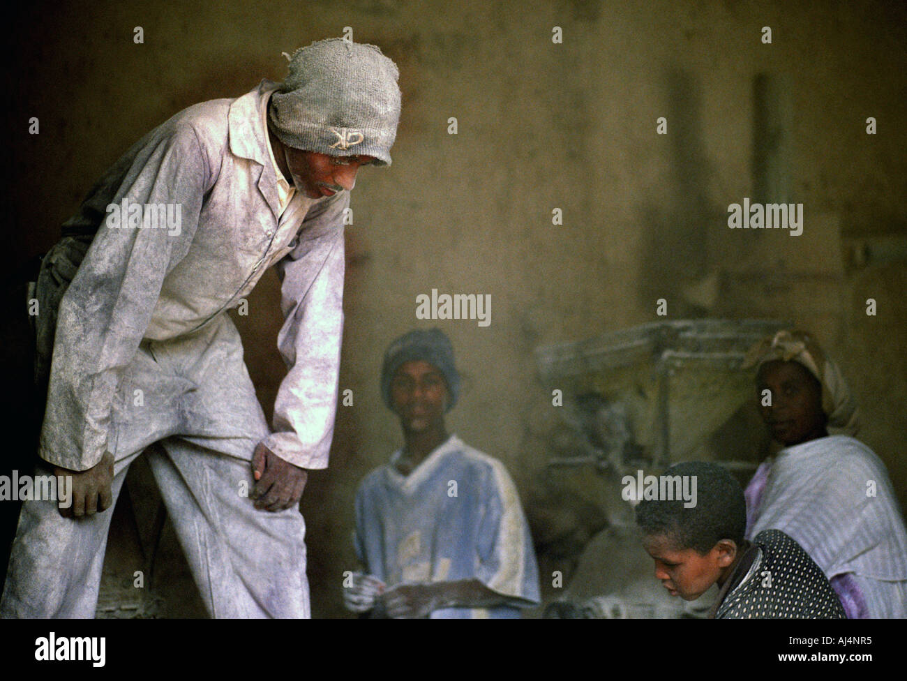 A young man covered in white flour dust loads flour at a mill while ...