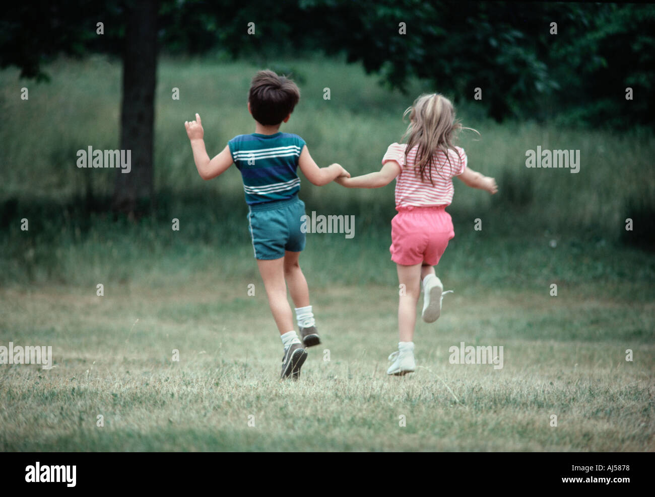 Little Caucasian boy and girl skipping in meadow Stock Photo - Alamy