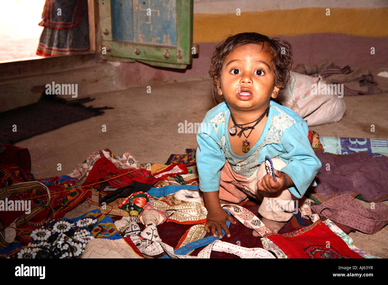 Harijan Tribal child crouching on ground with surrounding fabrics in ...