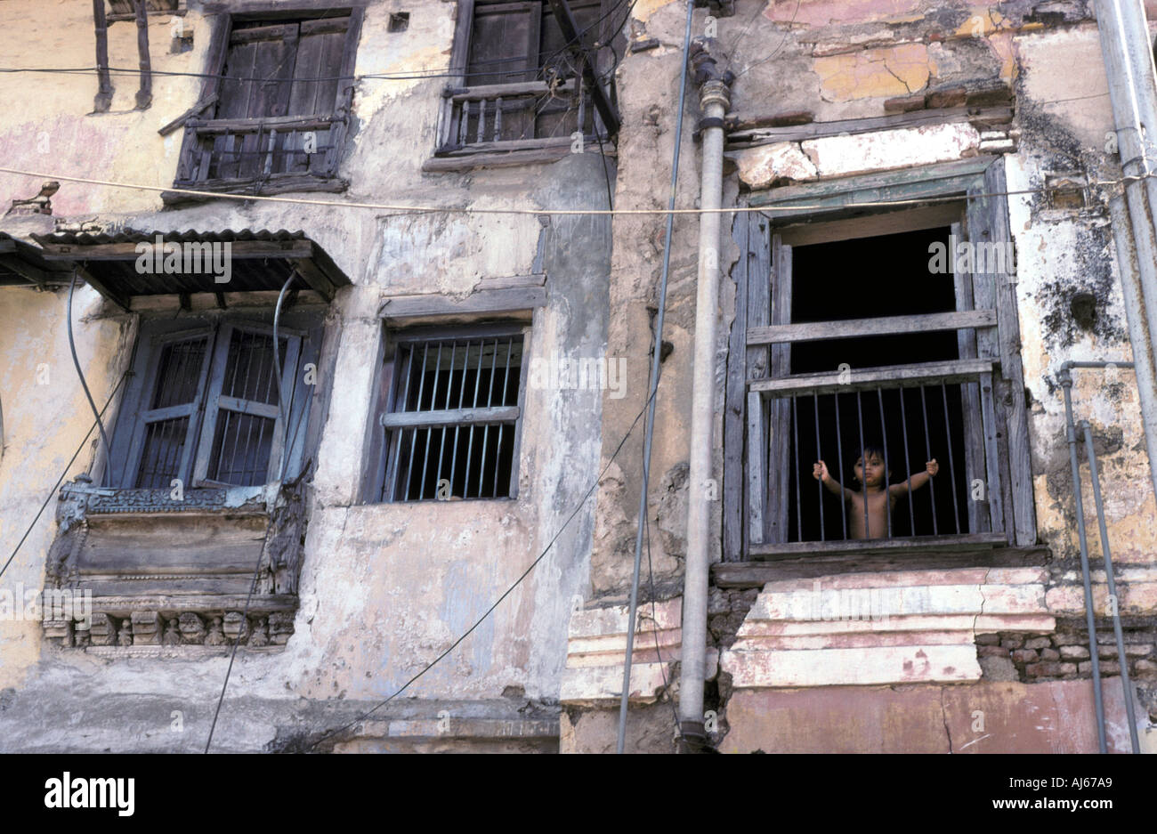 Indian child looking through bars on a window in a dilapidated building ...
