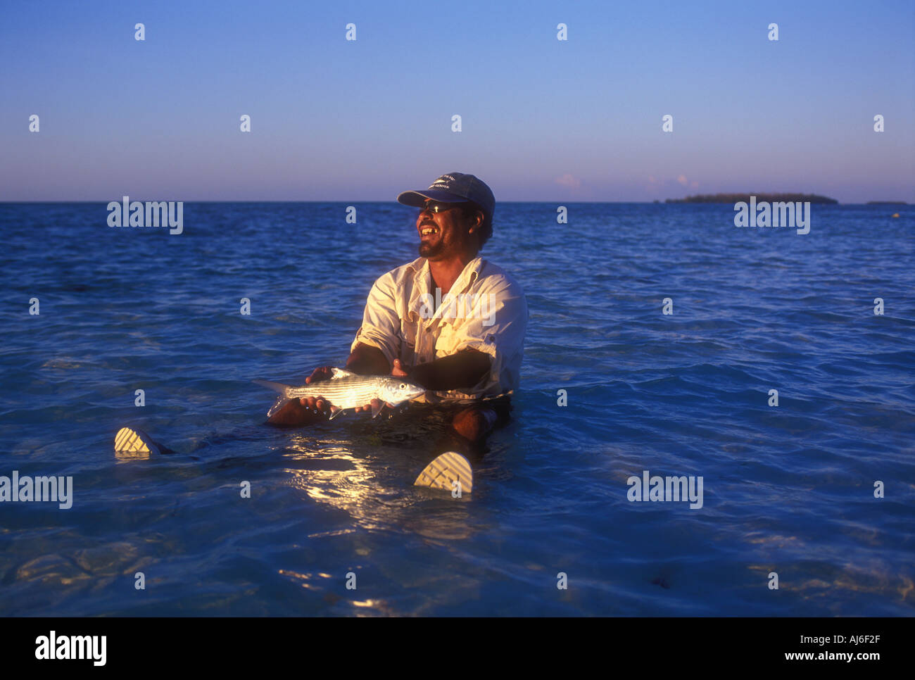 Man sitting in shallow water holding bonefish caught while fly fishing ...