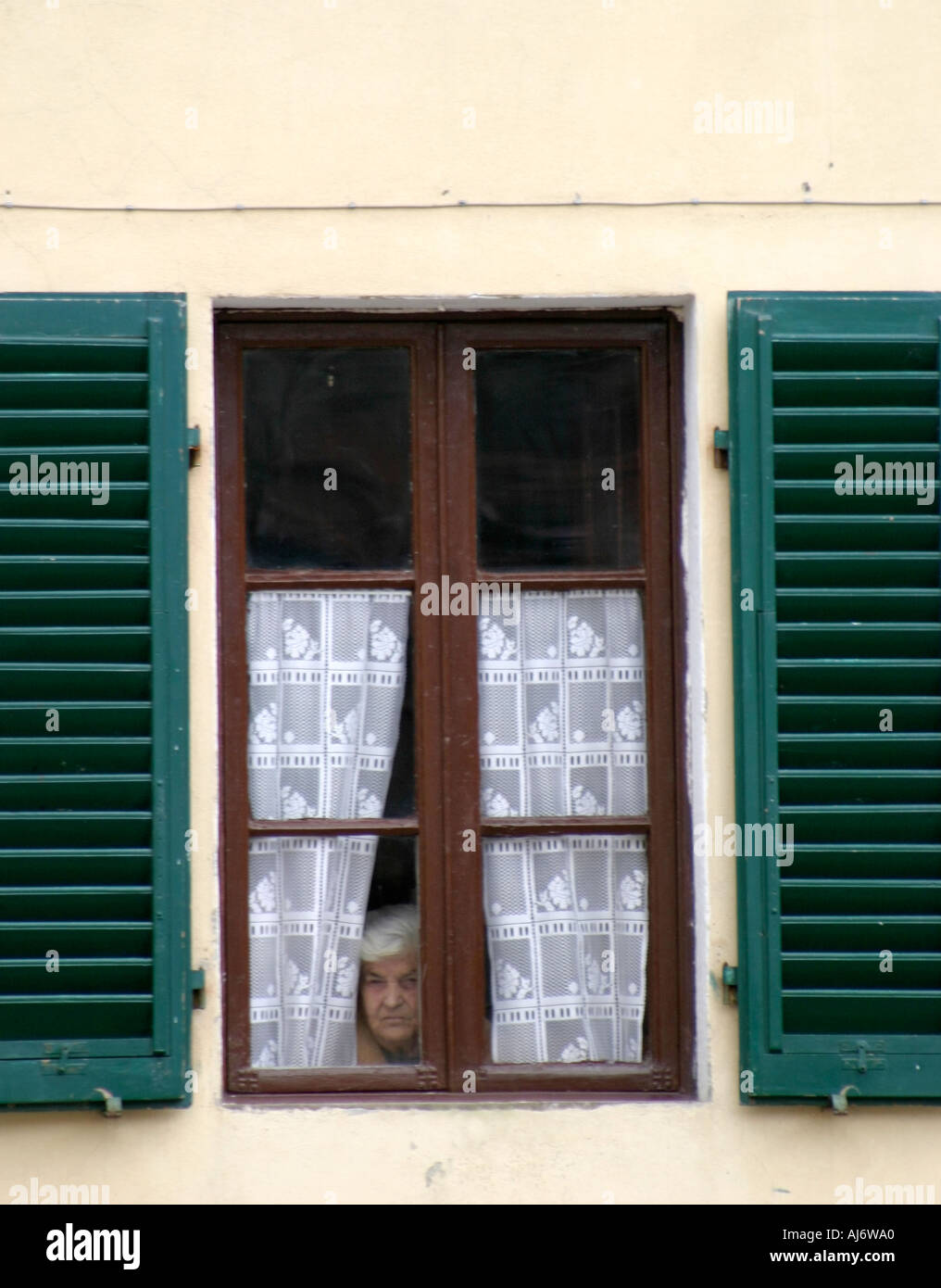 Elderly woman peeking out window Italy Stock Photo - Alamy