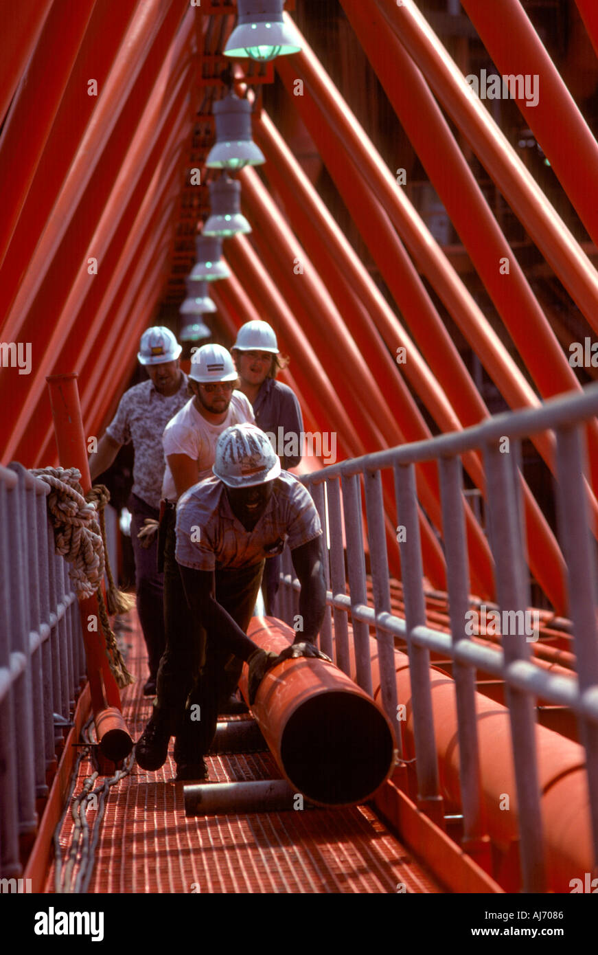 Workers rolling pipe across offshore platform bridge Stock Photo - Alamy