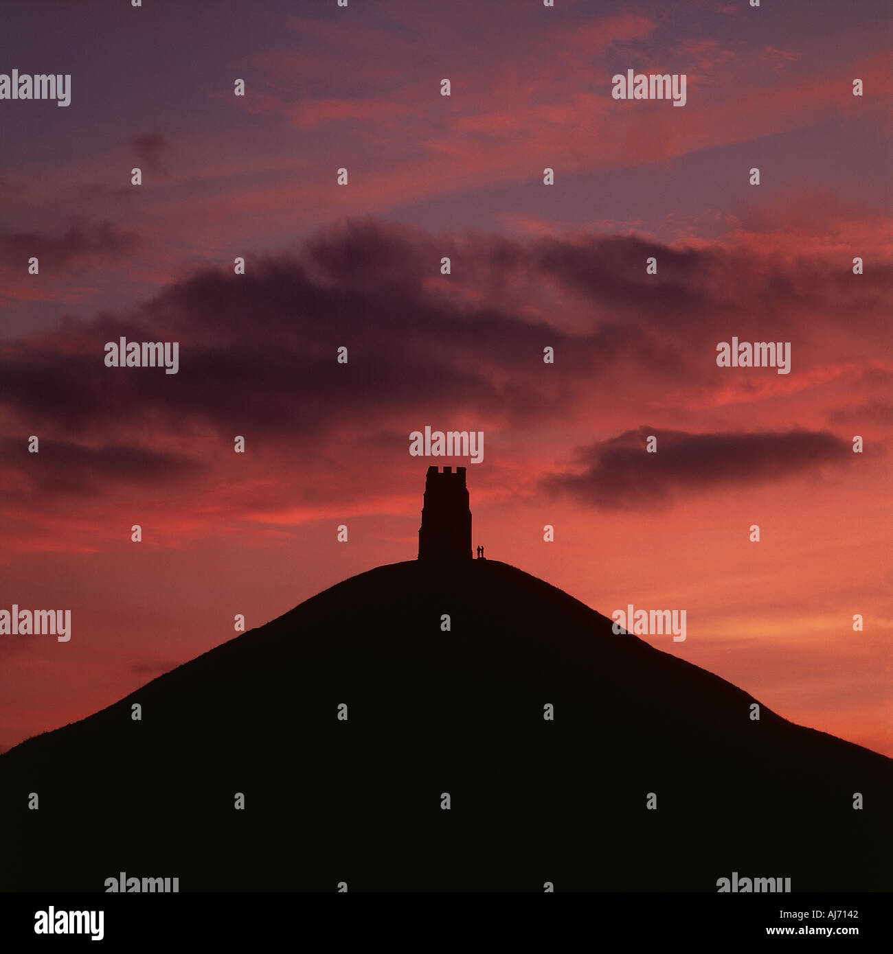 Glastonbury Tor in silhouette at Sunset, with two figures on hilltop ...