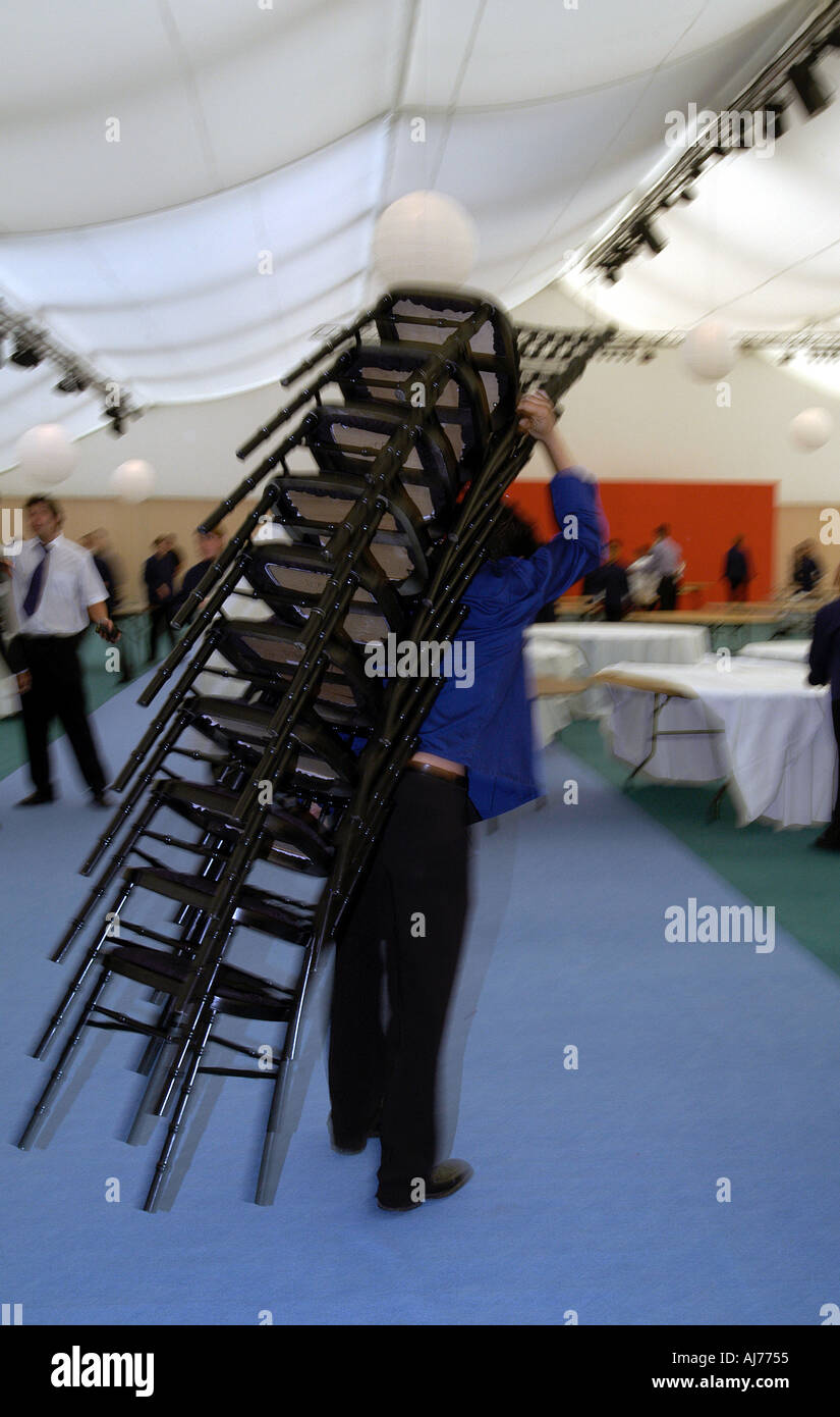 Waiter carrying stack of chairs through marquee Stock Photo - Alamy