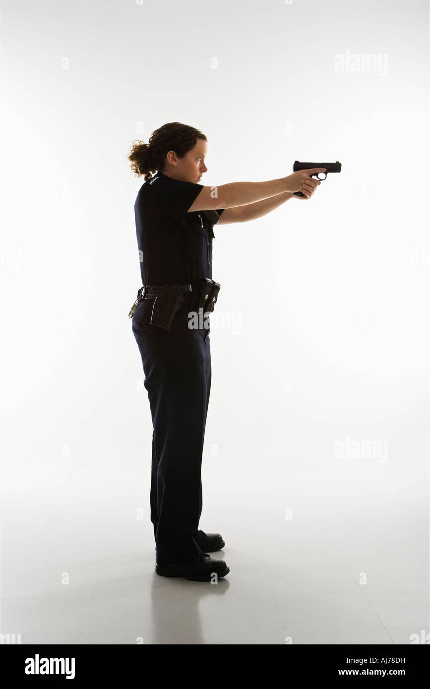 Side view of mid adult Caucasian policewoman standing and aiming ...