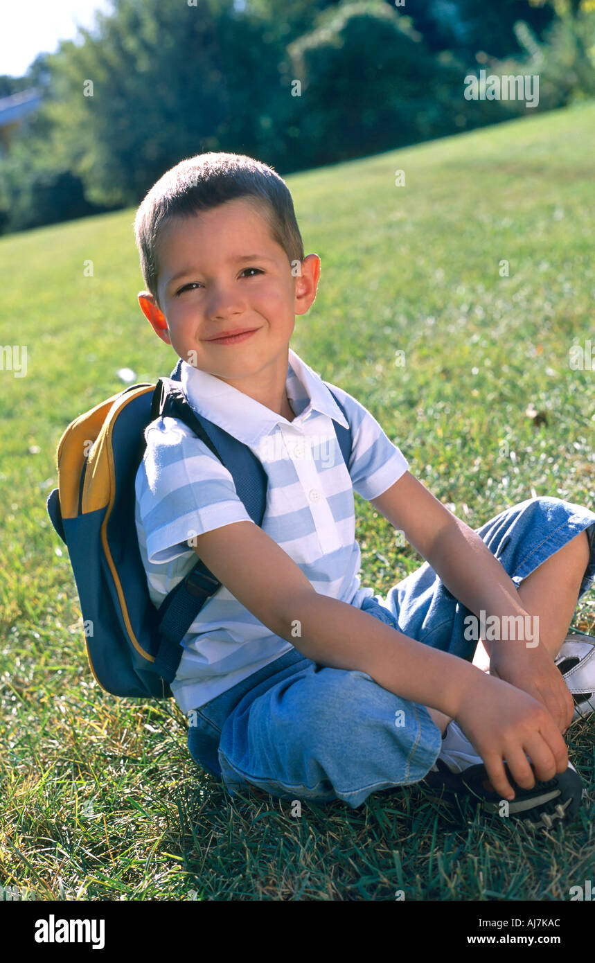 child boy schoolboy knapsack jeans sit sitting grass smile smiling ...