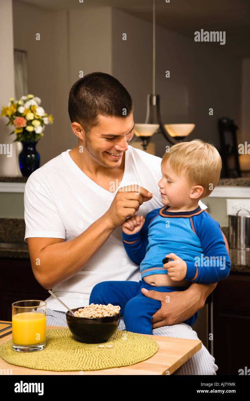 Caucasian man feeding toddler son on lap in kitchen Stock Photo - Alamy