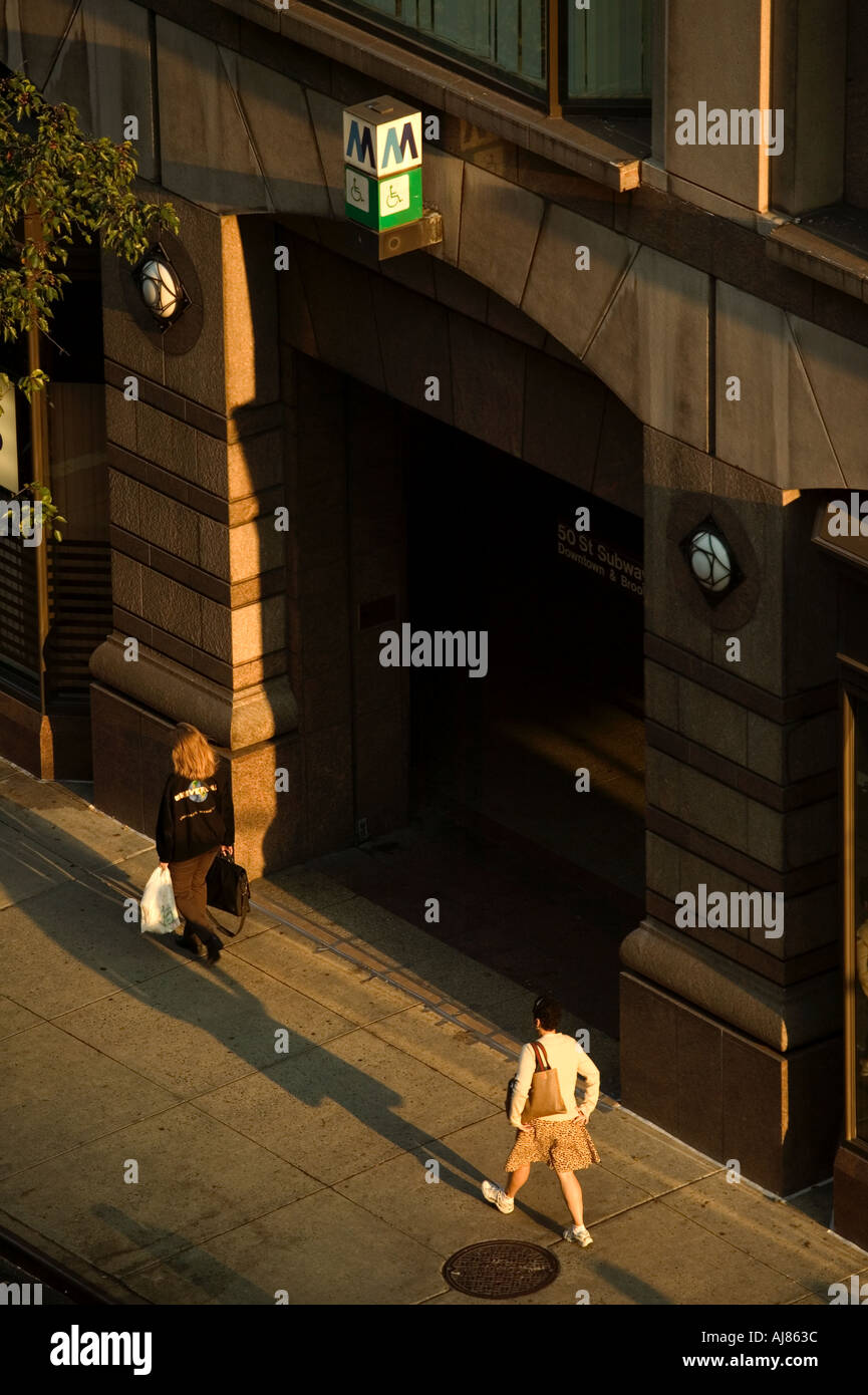 People walk in early morning sun light on sidewalk near Metro subway ...