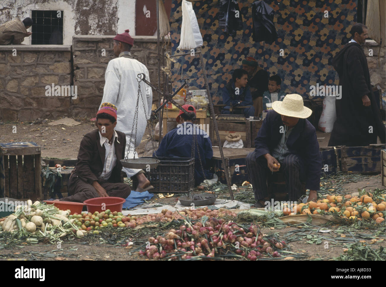 A few stallholders wearing hats sitting round piles of fruit and ...