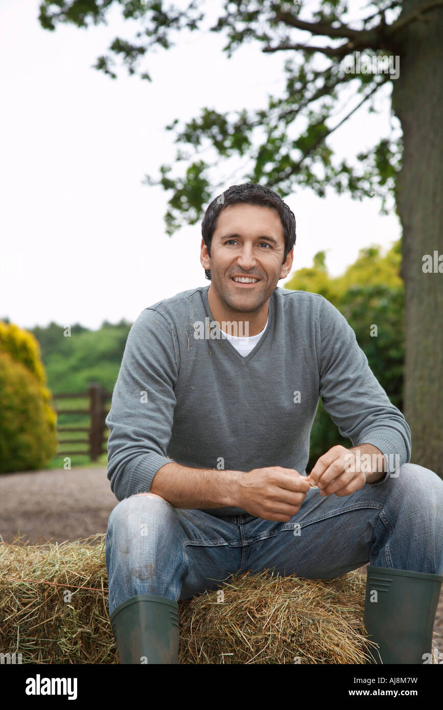 Man sitting on hay bale in countryside, portrait Stock Photo - Alamy