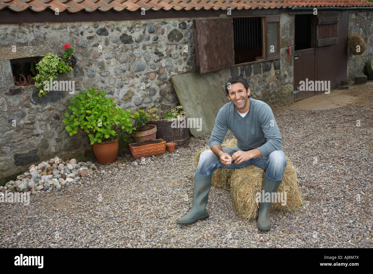 Man sitting on hay bale outside stable, portrait Stock Photo - Alamy