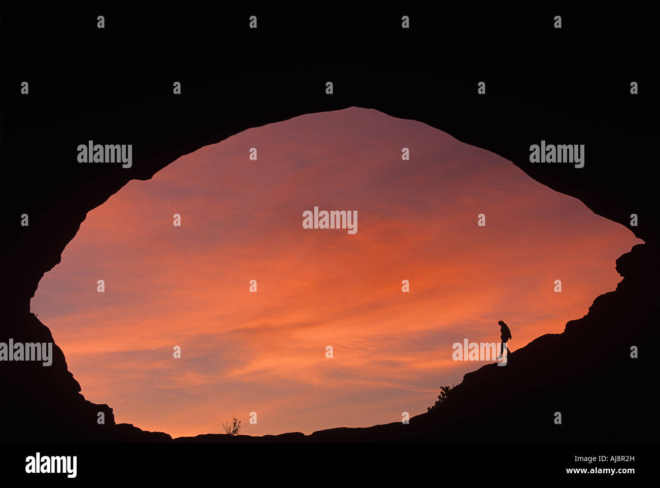 USA Utah Arches National Park Hiker climbs along edge of natural arch ...