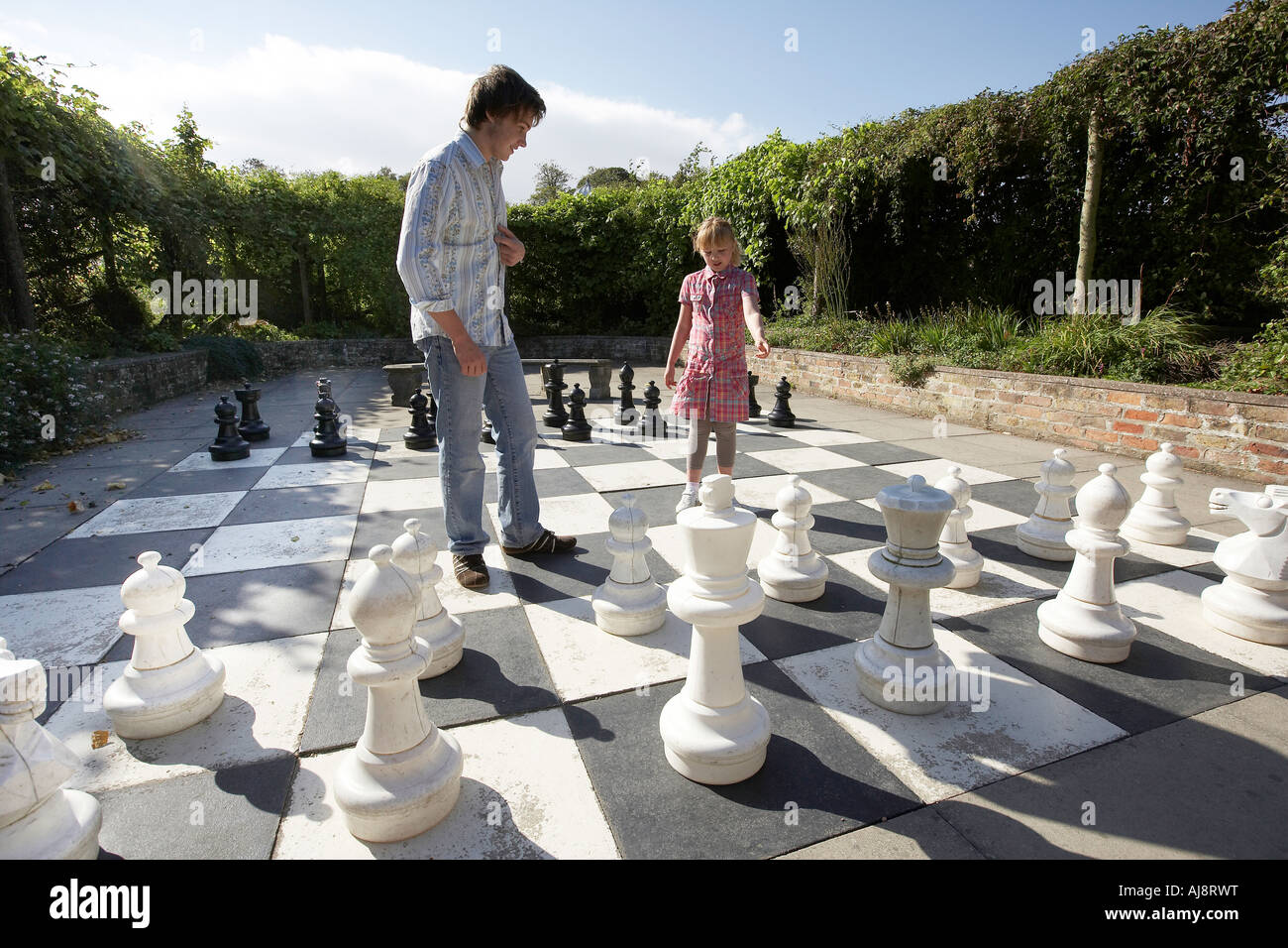 Girl aged 9 and boy aged 15 playing chess on a giant set in the grounds ...