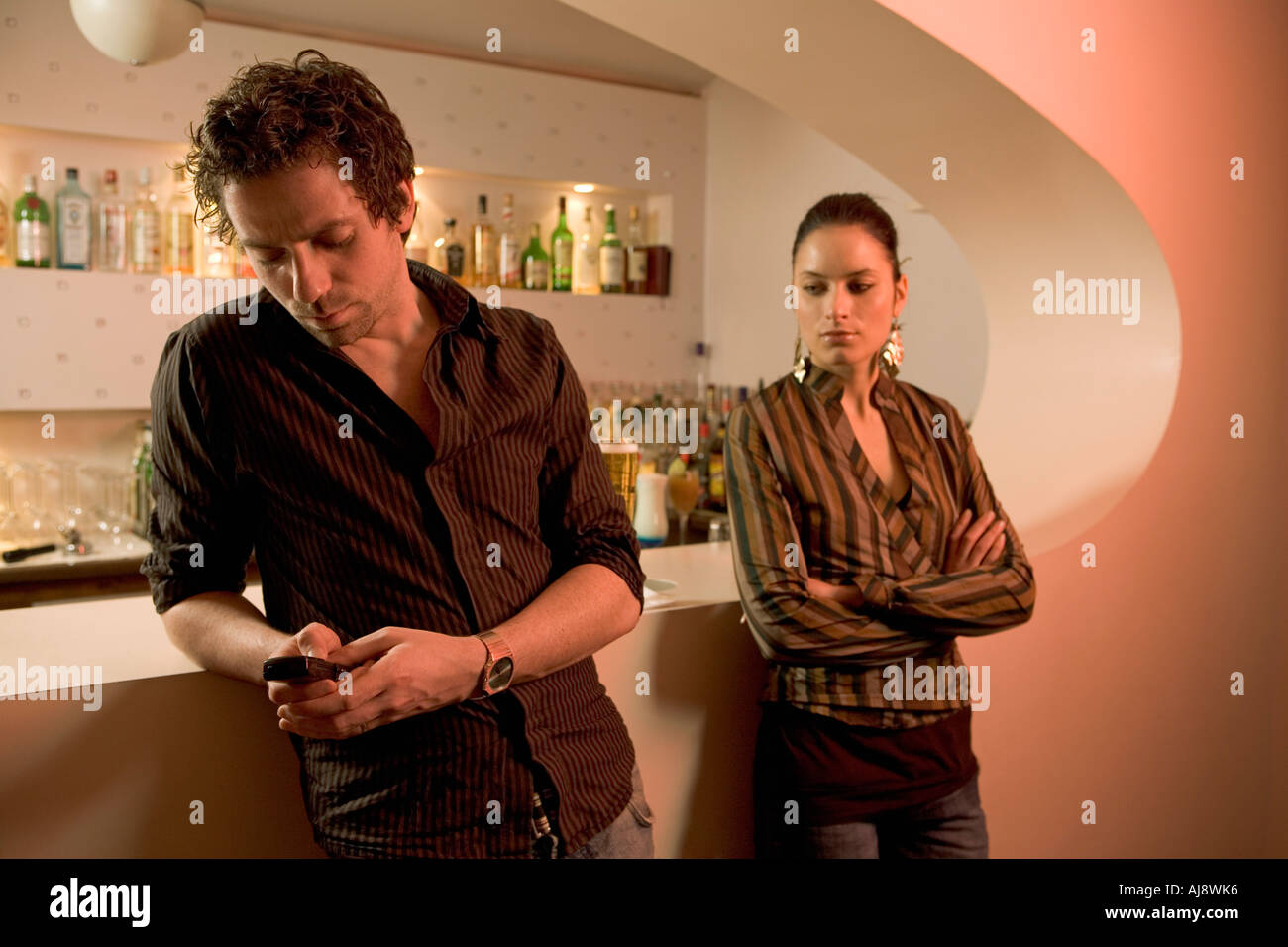 Man leaning against bar counter text messaging while woman is standing ...