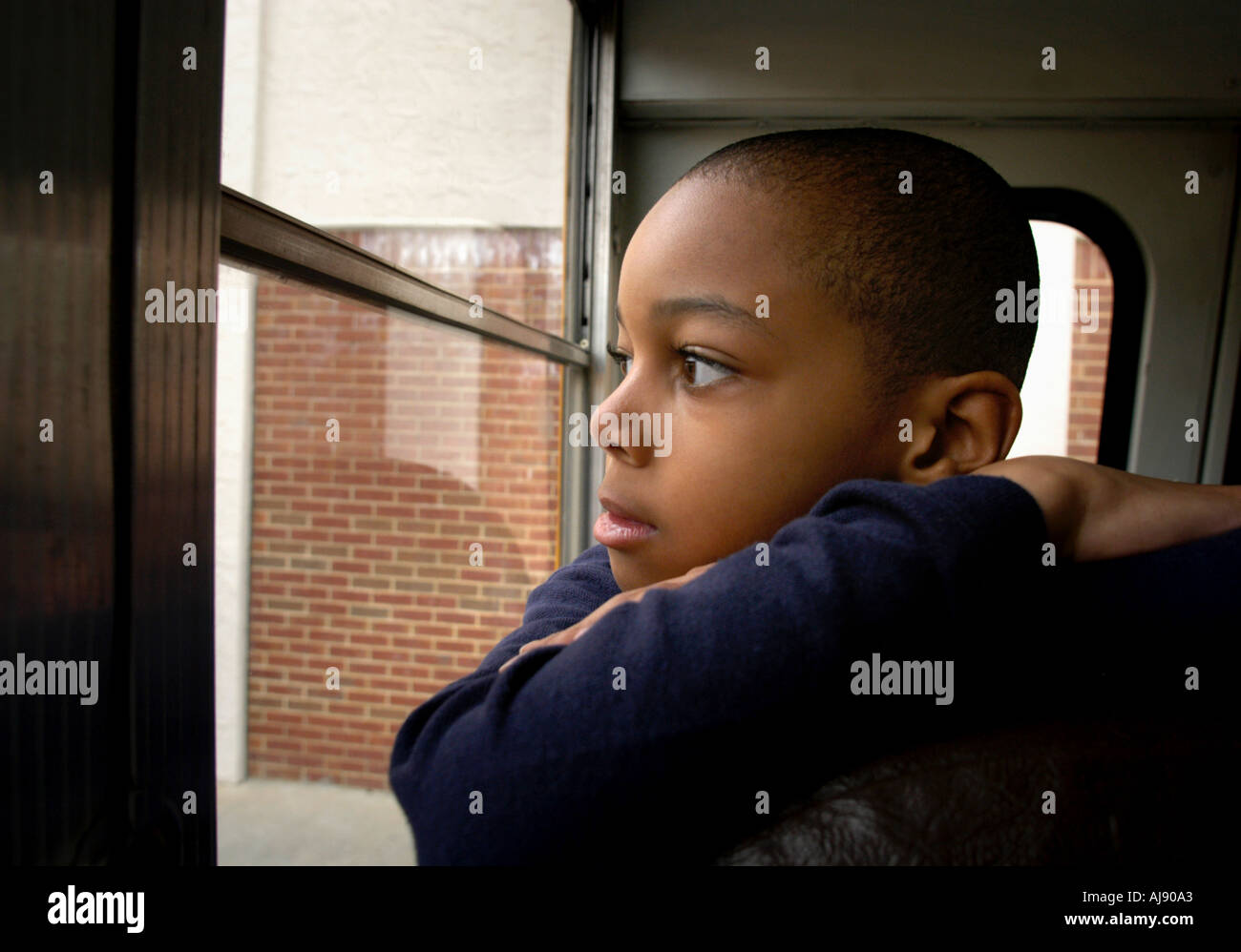 1st Grade black student boy sits in the back of school bus looking out ...
