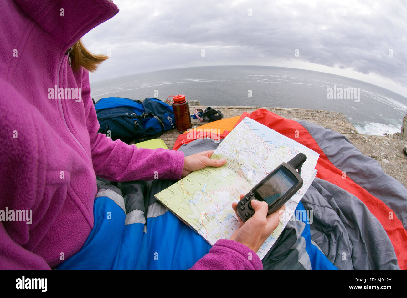 Reading map & GPS at camp on rocky ocean cliff Stock Photo - Alamy